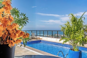 Piscina no terraço com vista para o oceano, cercada por plantas em vasos e uma espreguiçadeira.