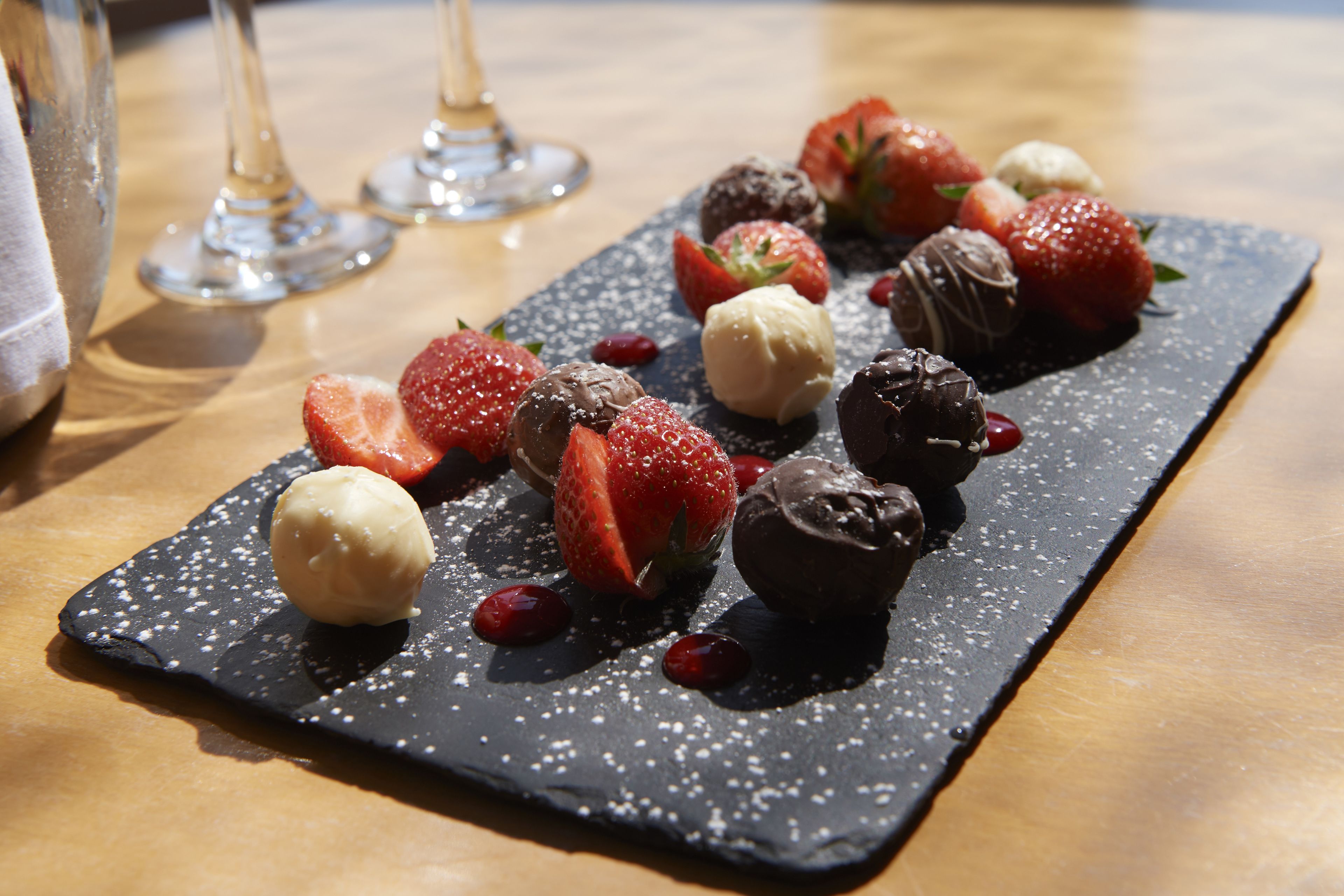 Um prato de sobremesa com morangos, chocolate e creme sobre uma lousa.