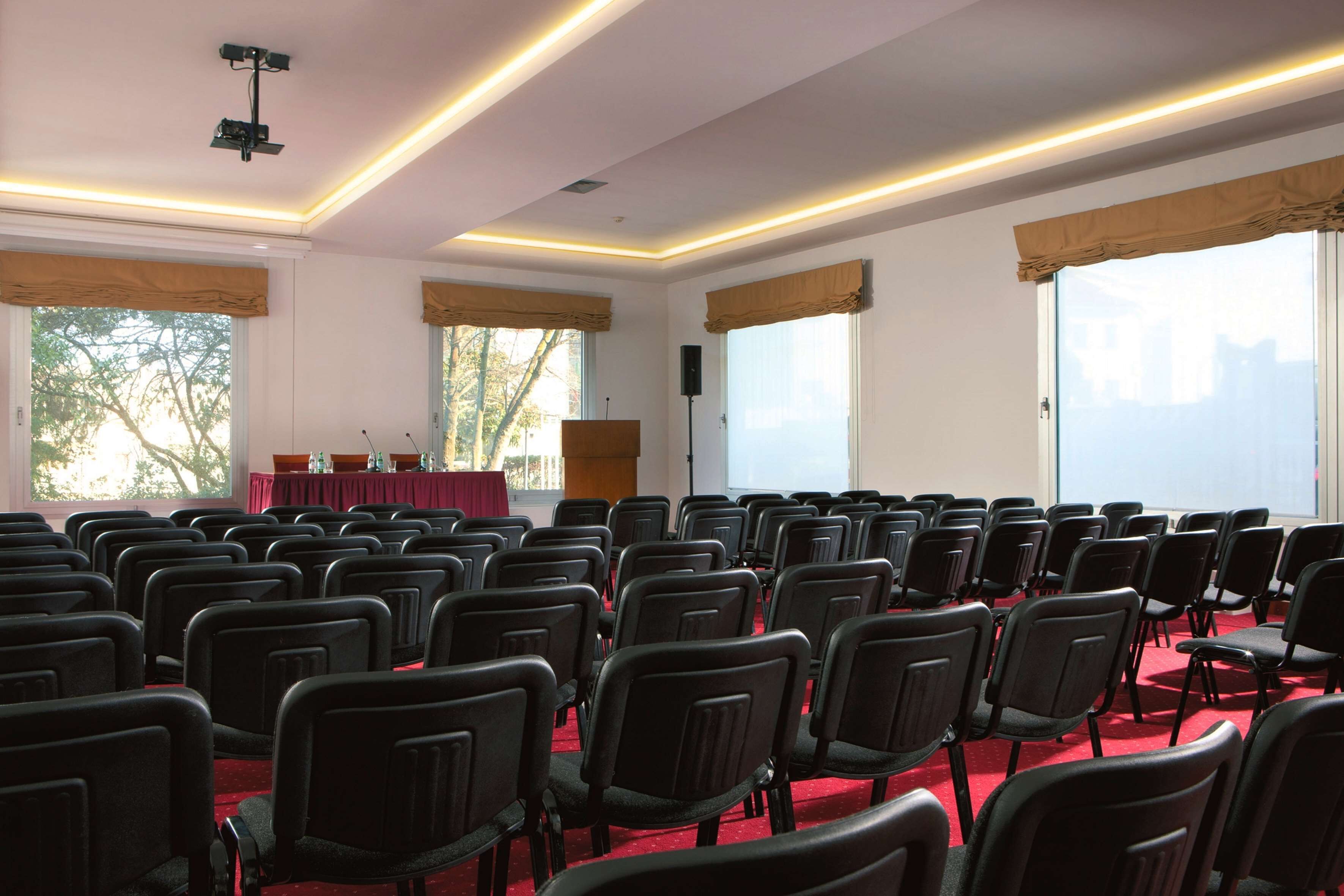 Uma sala de conferências com fileiras de cadeiras, um púlpito e um projetor.