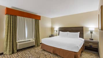 Quarto de hotel com uma cama grande, duas mesas de cabeceira com abajures, uma janela com cortinas e um tapete estampado.