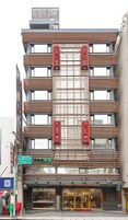Um edifício com vários andares, fachada moderna, janelas amplas e entrada no nível da rua com porta de vidro.