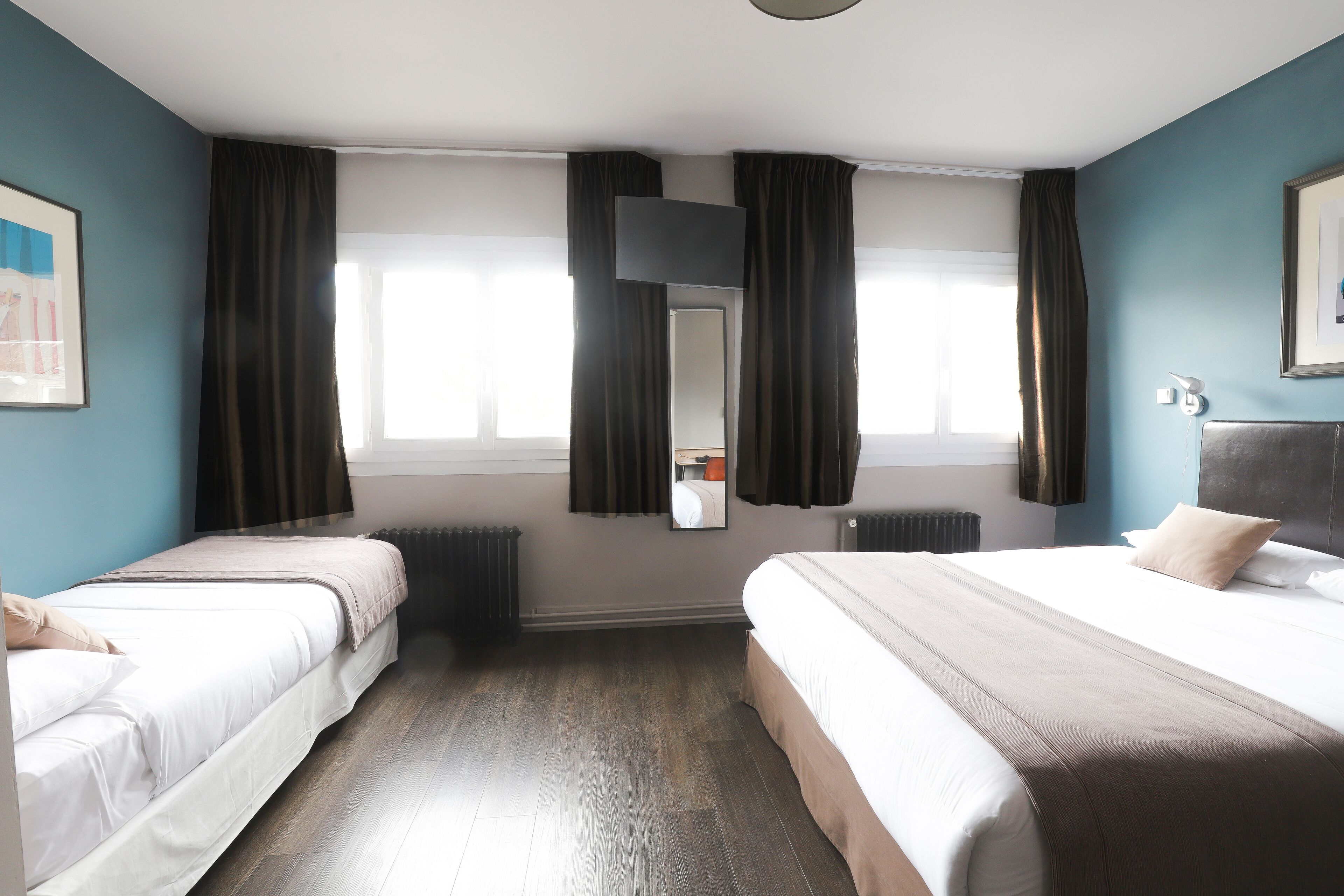 Quarto de hotel com duas camas, um espelho grande e uma janela com cortinas.