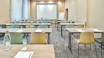 Uma sala de conferência com várias mesas, cadeiras, um projetor e um quadro branco.