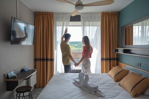 Quarto de hotel com cama, escrivaninha, televisão e vista para o exterior.