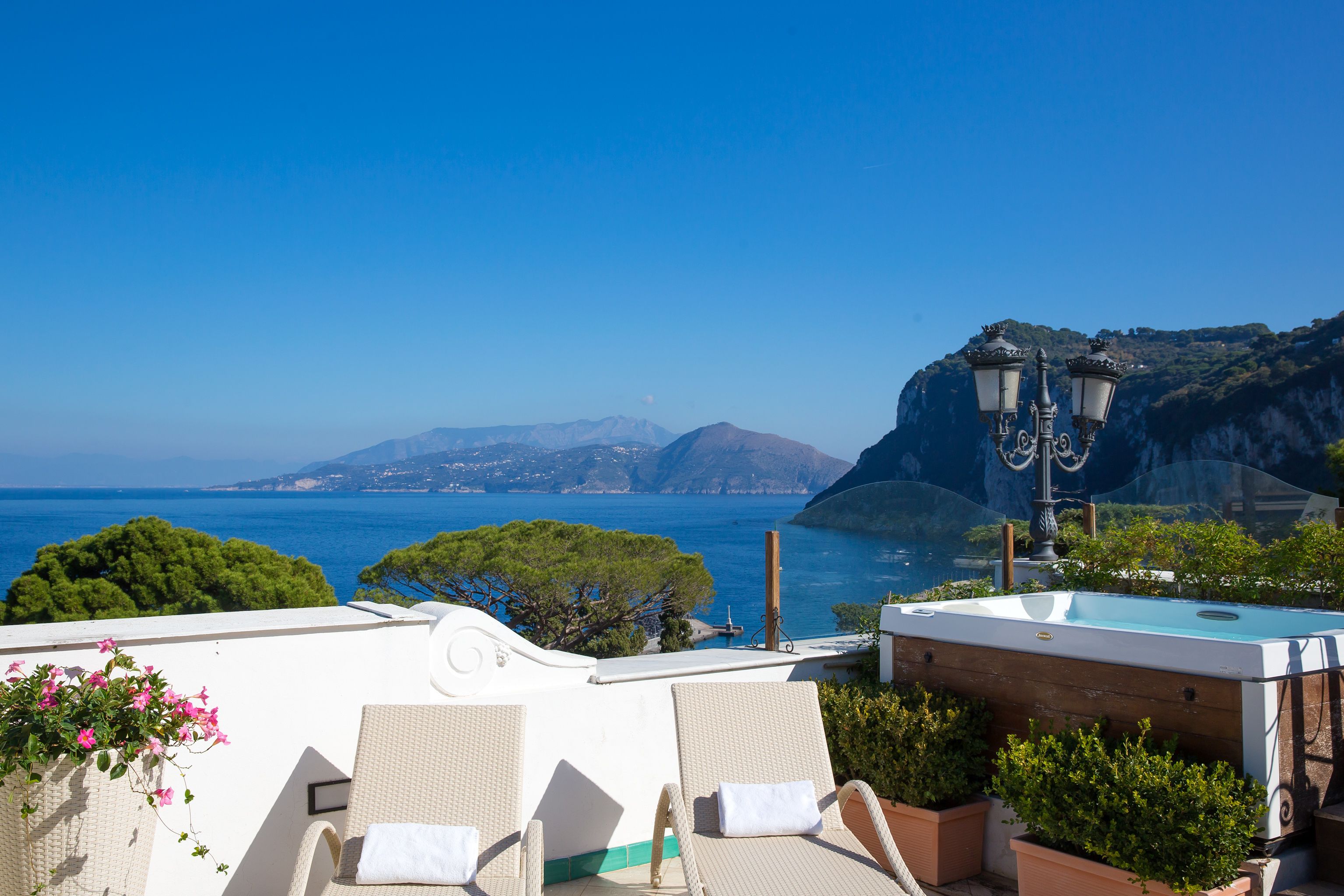 Terraço no telhado com piscina, cadeiras de descanso e vista para o mar e montanhas.