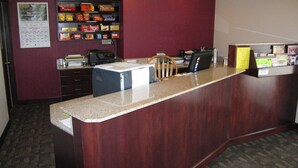 Uma mesa de recepção com computador, impressora e uma prateleira com lanches.