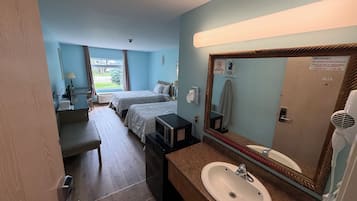 Quarto de hotel com duas camas, banheiro com pia e espelho, e janela com cortinas.