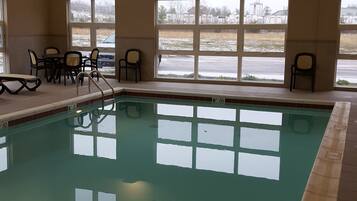 Piscina interior com janelas amplas, cadeiras e vista para o exterior.