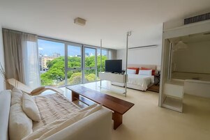 Quarto de hotel moderno com uma janela grande, uma cama, uma mesa de cabeceira, uma televisão e um guarda-roupa.