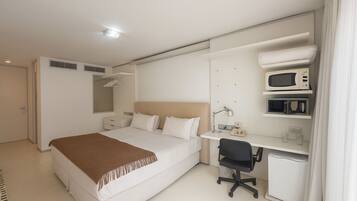 Quarto de hotel com cama, escrivaninha, cadeira e micro-ondas.