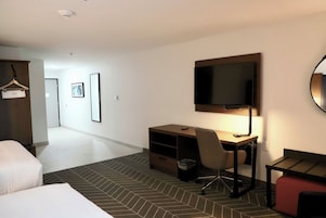 Quarto de hotel com uma cama, uma escrivaninha com cadeira, televisão e guarda-roupa.