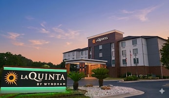 Placa de hotel com 'LA QUINTA BY WYNDHAM' e um edifício moderno com várias janelas e uma bandeira.