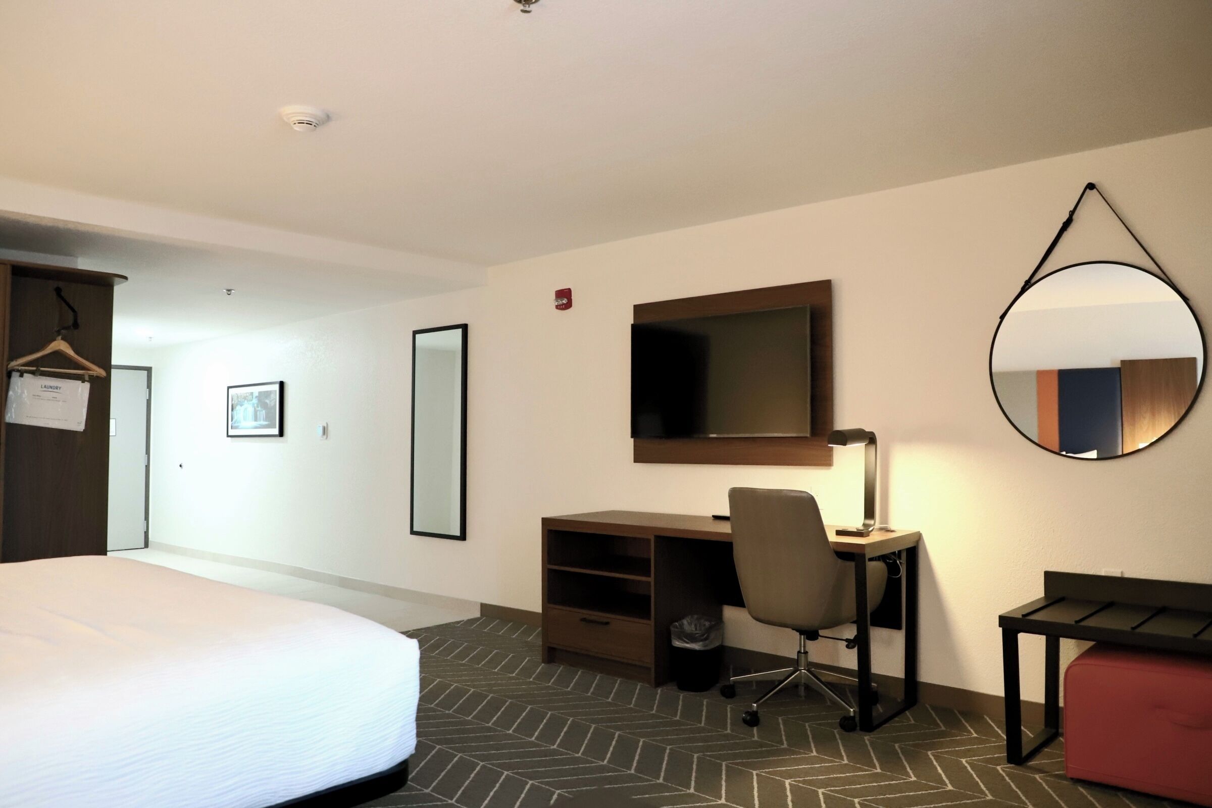Quarto de hotel com cama, escrivaninha com cadeira, televisão, espelho e armário.