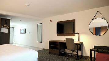 Quarto de hotel com cama, escrivaninha com cadeira, televisão, espelho e armário.