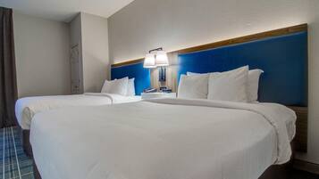 Quarto de hotel com duas camas, uma mesa de cabeceira com abajur e uma parede azul decorativa.