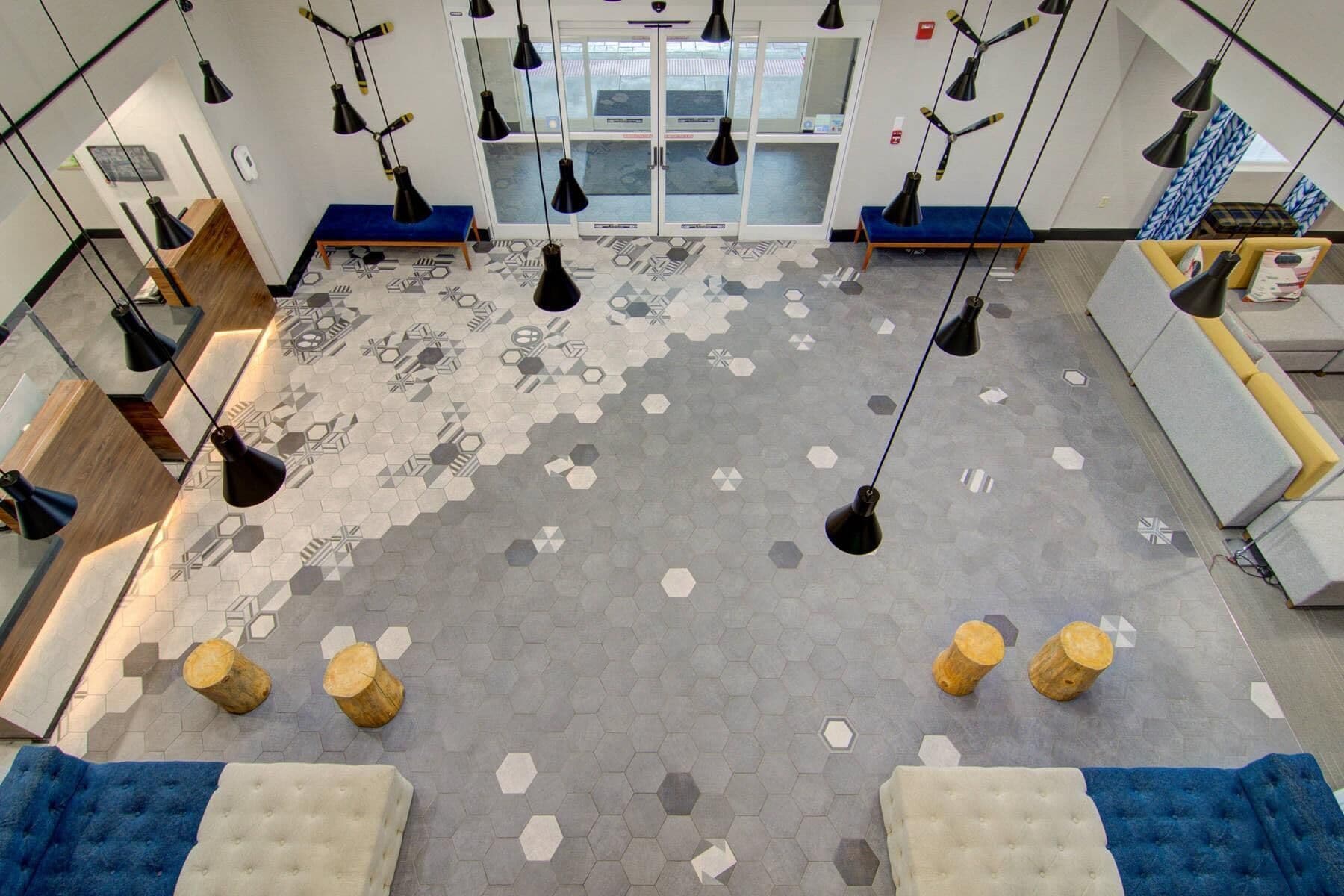 Um hall amplo com piso em padrão hexagonal, várias áreas de estar e iluminação pendente.