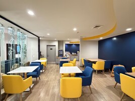 Uma área de refeições moderna com mesas e cadeiras, uma cozinha e um separador de vidro com detalhes decorativos.