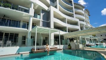 Um hotel moderno com área de piscina, várias varandas e um espaço de estar coberto.
