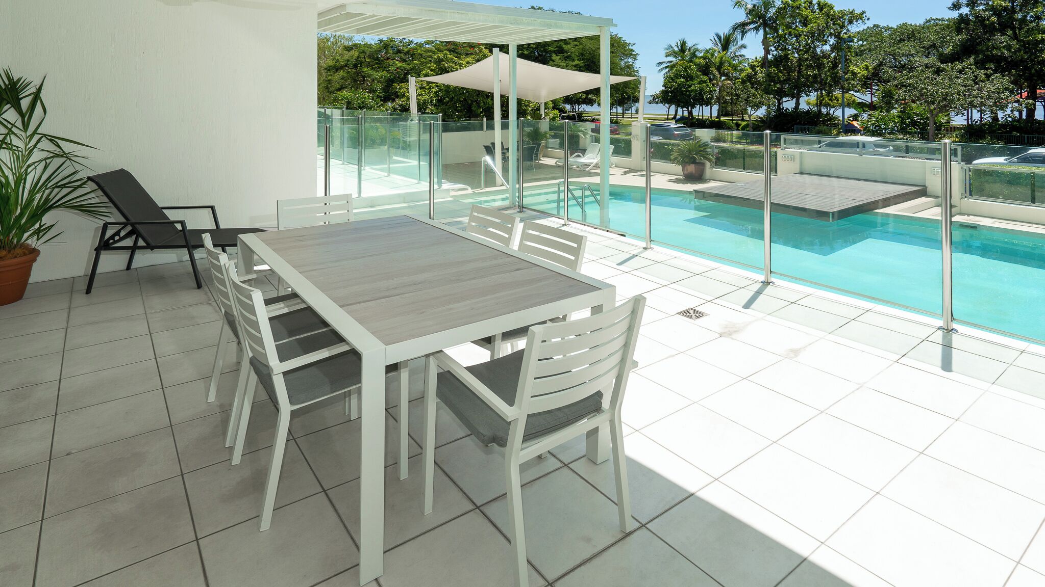 Um pátio moderno ao ar livre com piscina, móveis brancos e área de estar coberta.