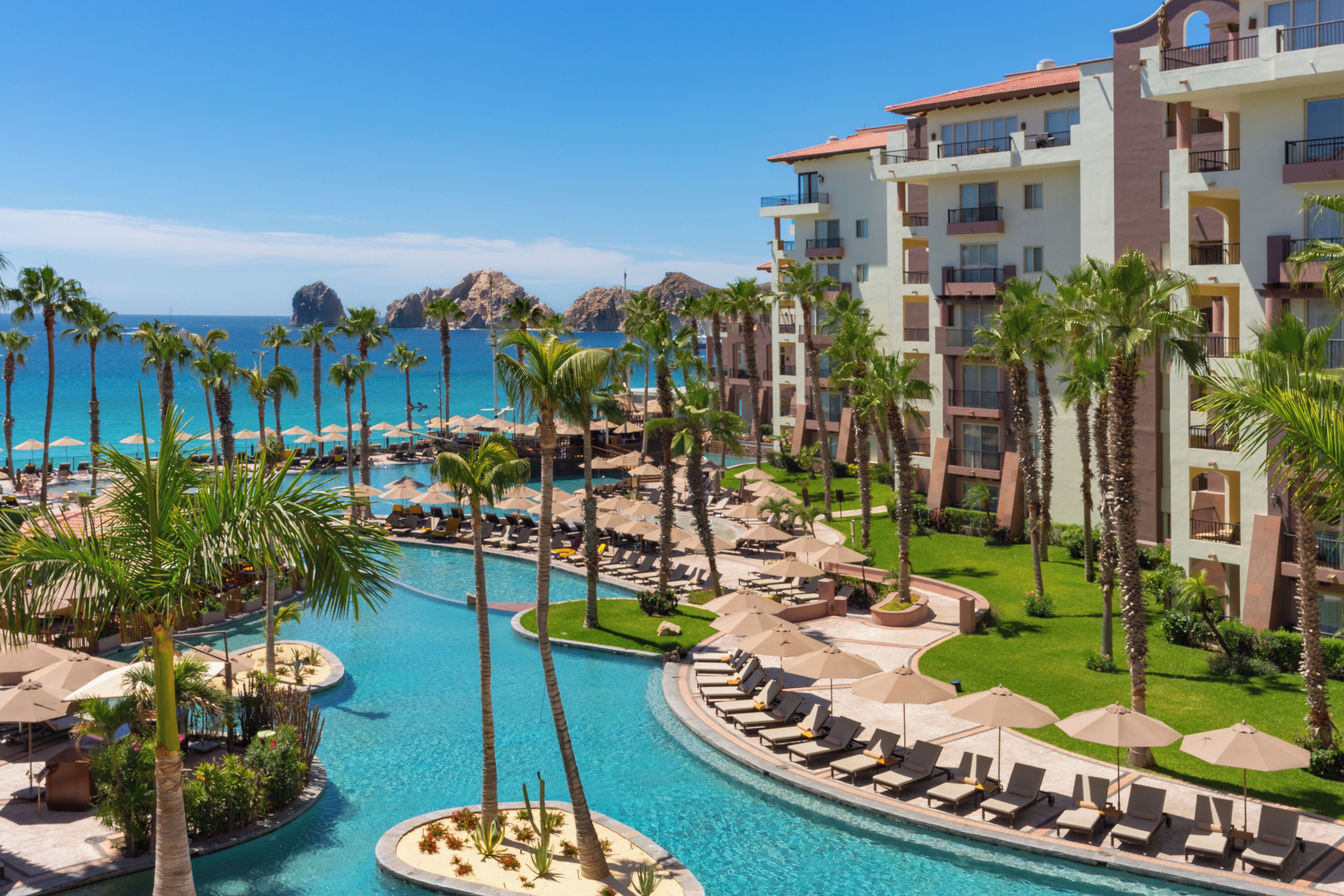 Um resort com uma piscina grande, palmeiras e vista para o oceano.