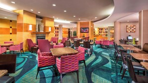 Um saguão de hotel com diversas áreas de estar, incluindo mesas e cadeiras, e uma lareira.