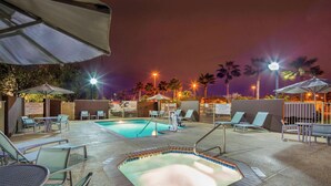 Área de piscina com espreguiçadeiras, banheira de hidromassagem e guarda-sóis.