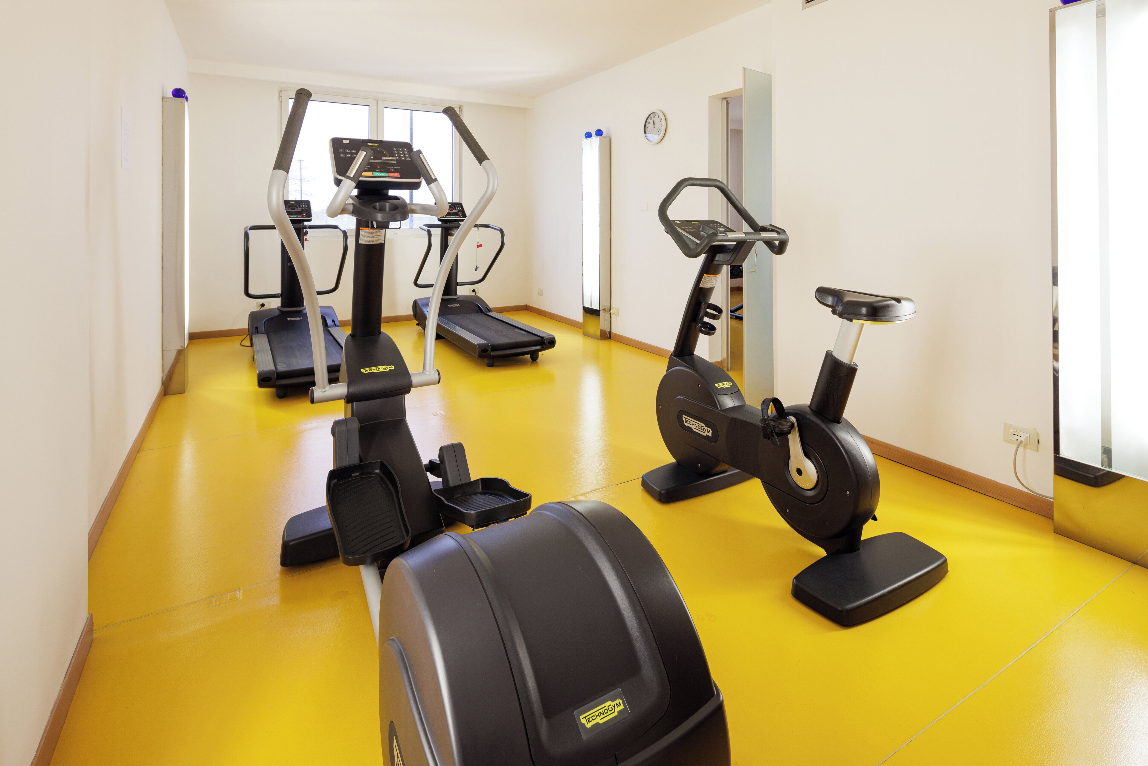 Uma sala de ginástica com bicicletas ergométricas e esteiras.