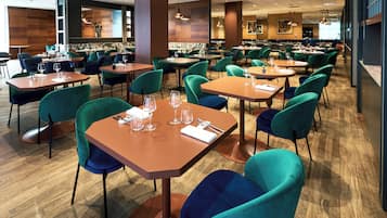 Um restaurante moderno com várias mesas e cadeiras, com uma combinação de assentos de madeira e estofados.