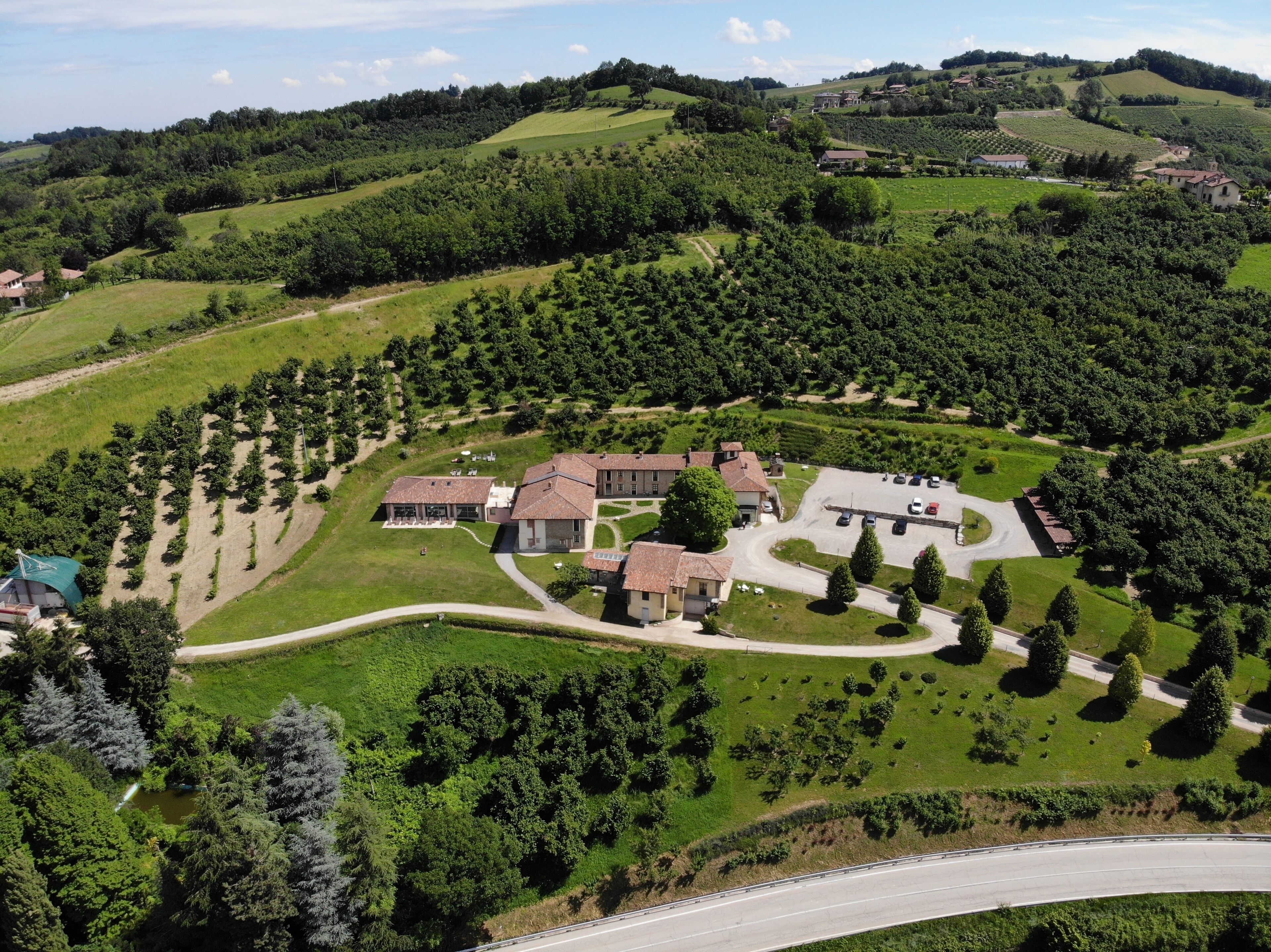 Vista aérea de um casarão rural cercado por vegetação exuberante, área de estacionamento e estrada sinuosa.