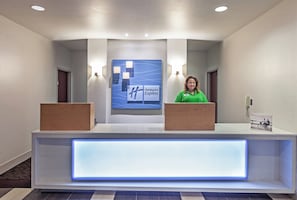 Uma mesa de recepção de hotel com design moderno, exibindo uma placa de identificação, uma tela digital e uma área de atendimento.