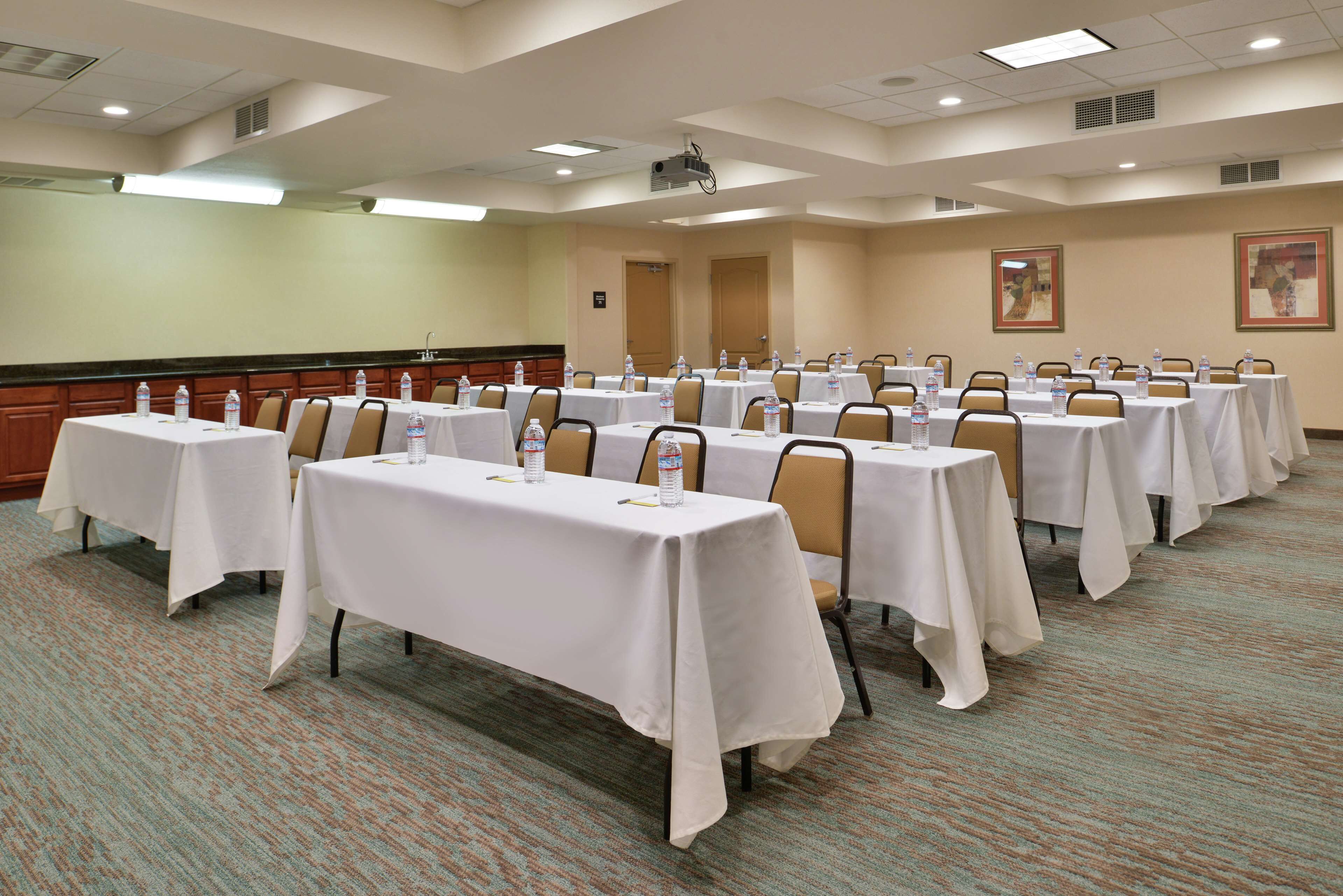 Sala de conferência com várias mesas, cada uma coberta por um pano de mesa branco, e equipada com garrafas de água.