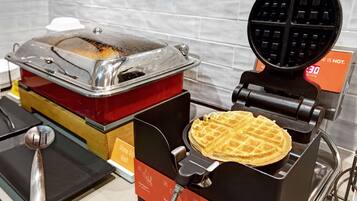 Uma máquina de waffles com um waffle dentro, uma colher de metal e uma placa com a inscrição 'Grill Rib Hash'.