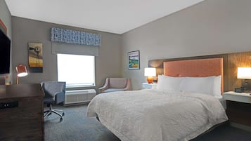 Quarto de hotel com uma cama grande, uma escrivaninha, uma cadeira, televisão e obras de arte nas paredes.
