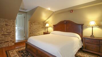 Quarto com cama grande, cabeceira de madeira, duas mesas de cabeceira com abajures, parede decorativa de pedra e uma porta que dá para outro quarto.