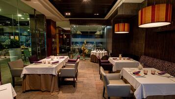 Um restaurante com várias mesas e cadeiras, um banco estampado e um muro de vidro com vista.