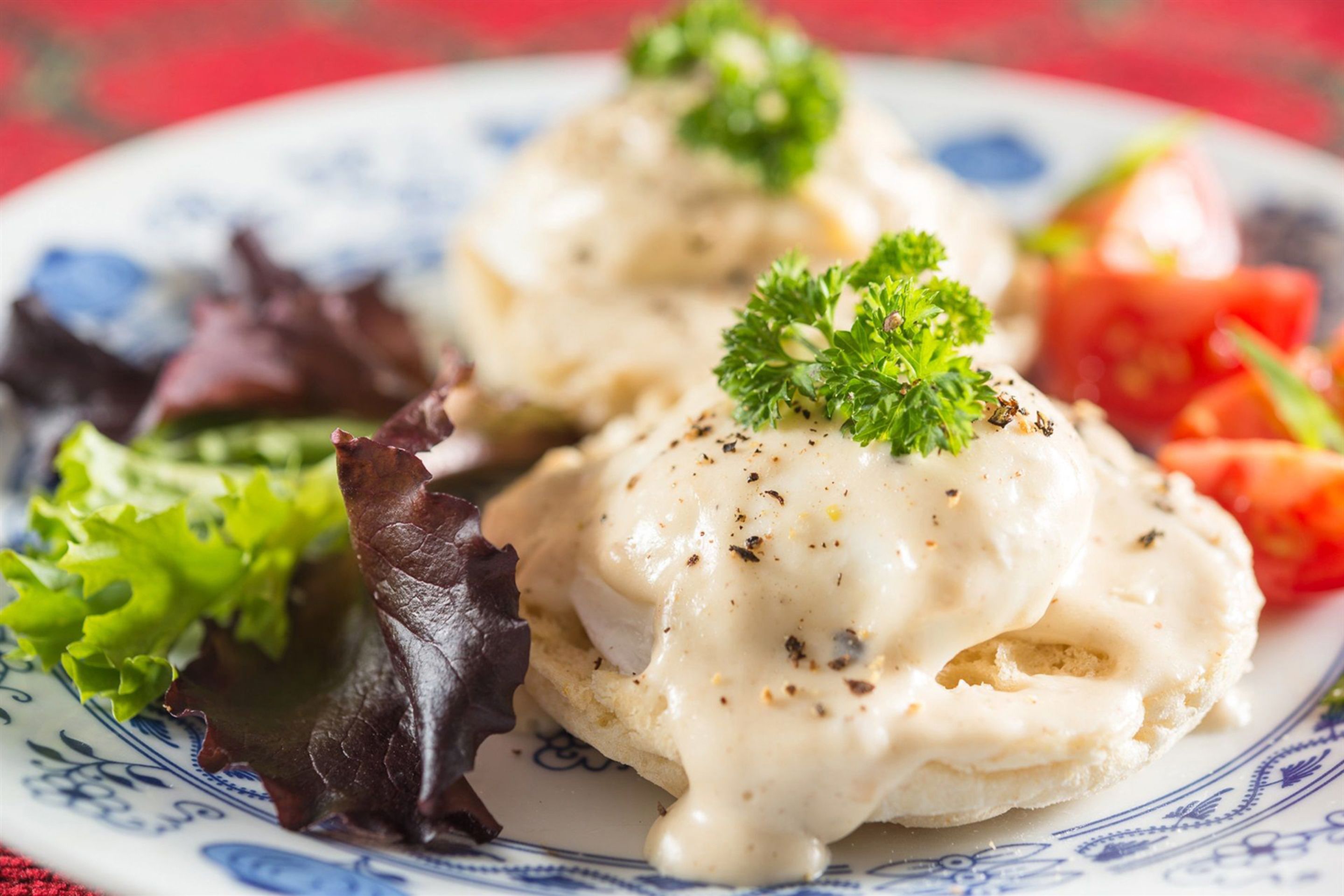 Um prato com dois ovos pochê, adornado com salsa, acompanhado de uma salada e tomates fatiados.
