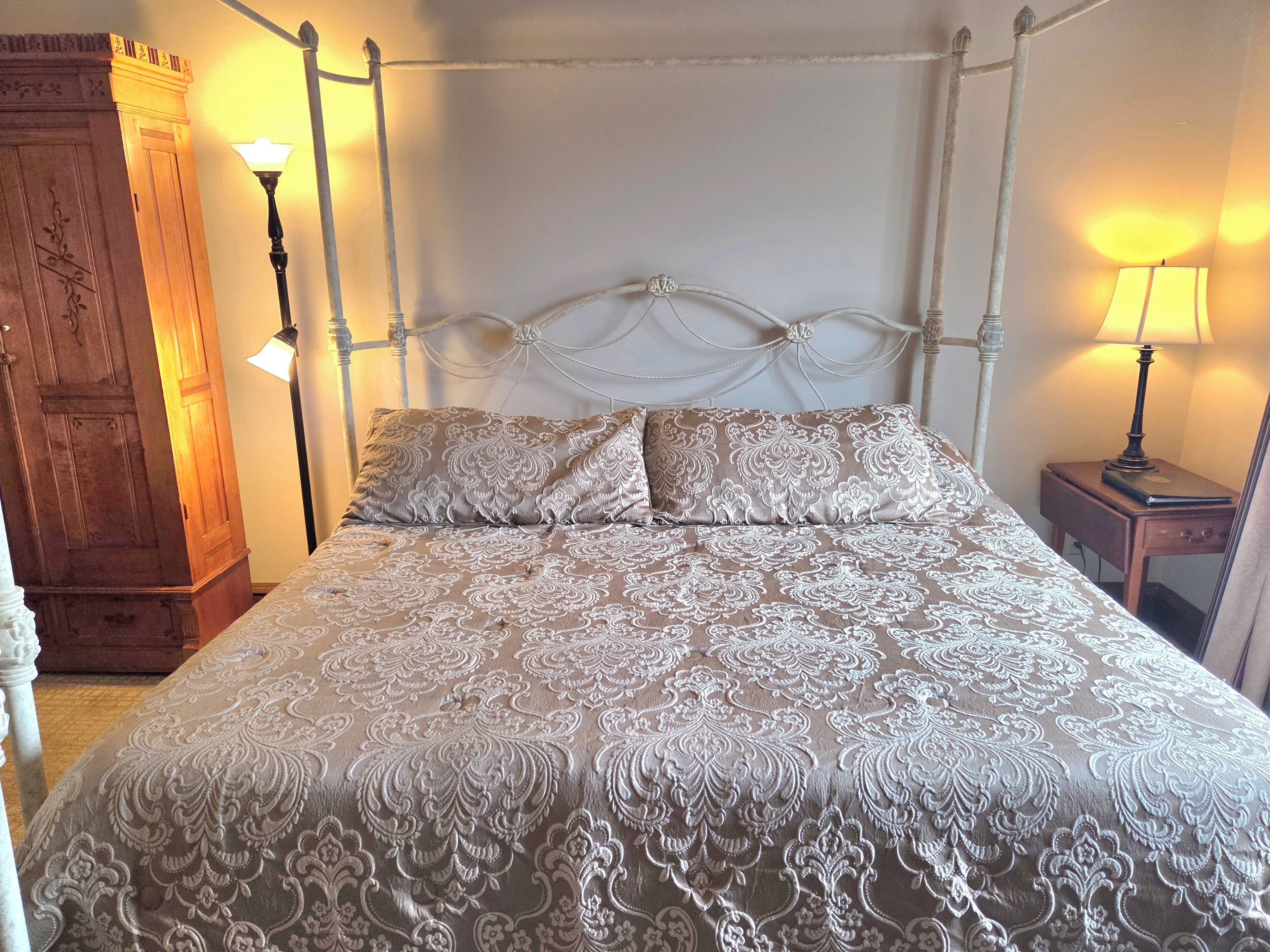 Uma cama com cabeceira branca e elaborada, duas luminárias de cabeceira e um guarda-roupa de madeira.