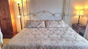 Uma cama com cabeceira branca e elaborada, duas luminárias de cabeceira e um guarda-roupa de madeira.