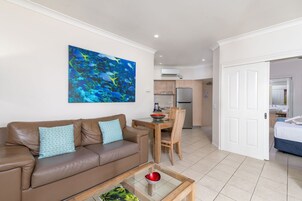 Um apartamento moderno com um sofá de couro marrom, uma mesa de jantar com cadeiras, uma área de cozinha e um quarto com cama.