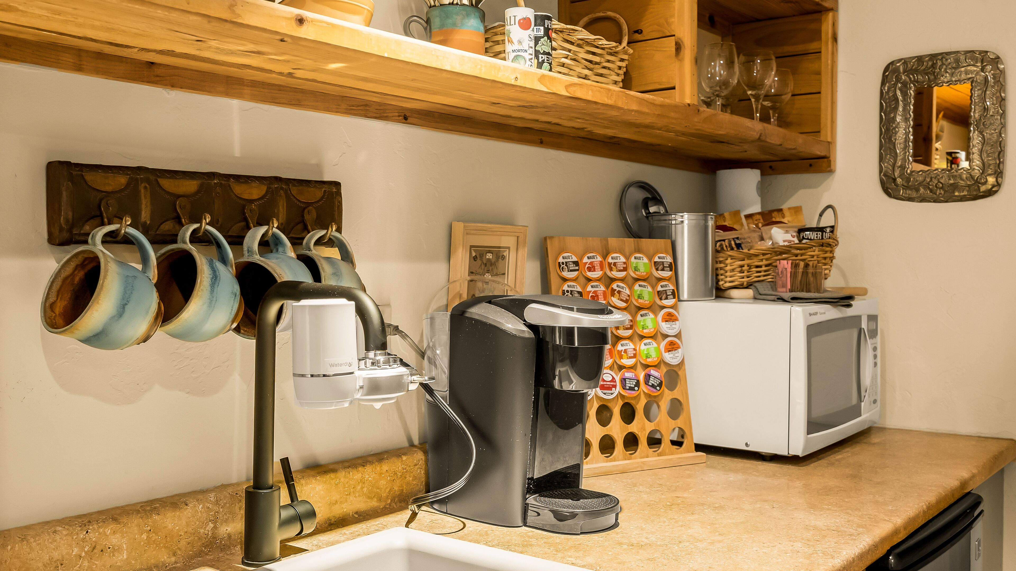 Uma cozinha com cafeteira, canecas, saleiro e pimenteiro, micro-ondas e uma prateleira de madeira com utensílios de cozinha.