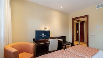 Quarto de hotel com cama, escrivaninha, computador, cadeira e televisão.