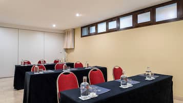 Sala de conferência com mesas preparadas para reuniões, equipada com garrafas de água e copos.