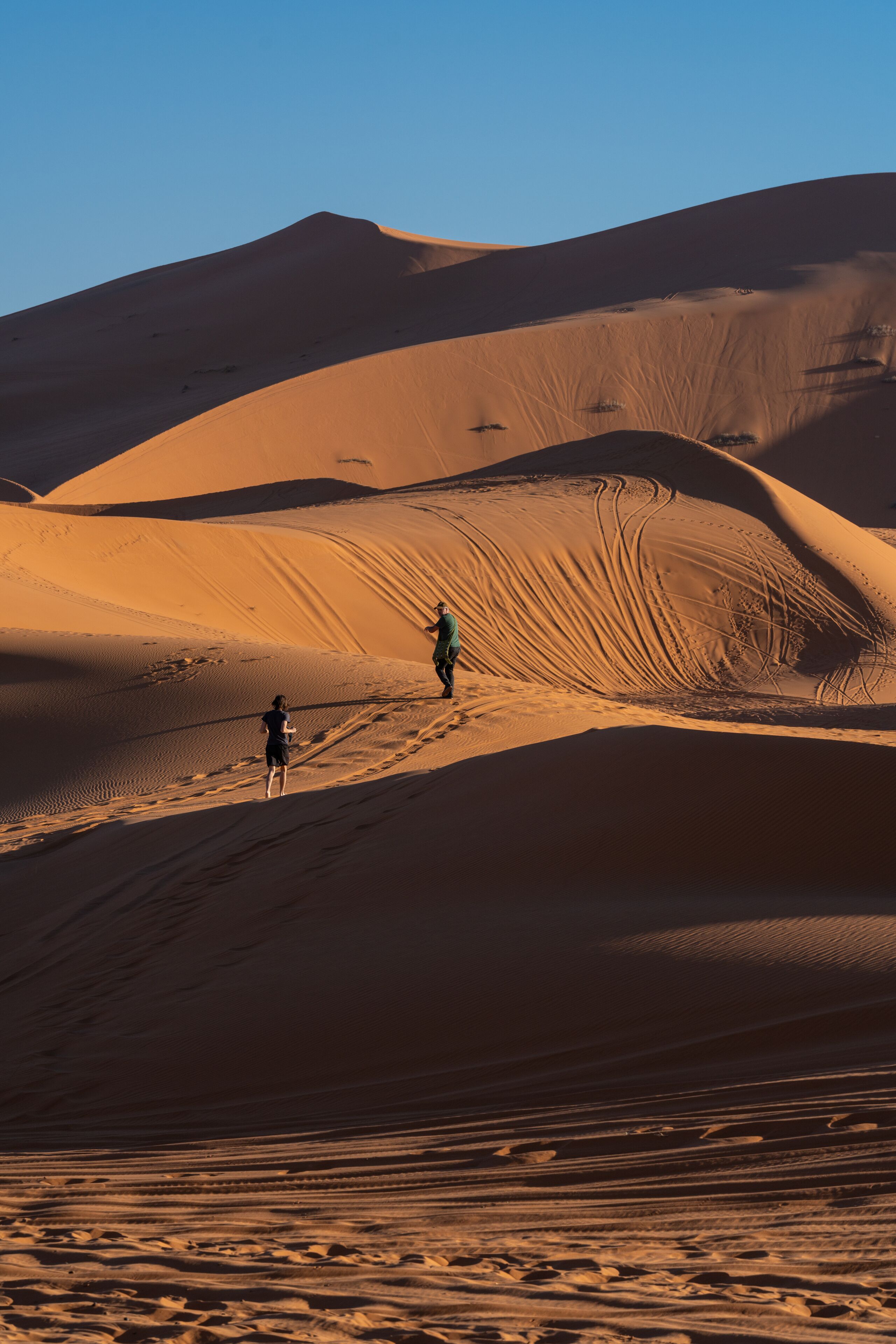 Paisagem desértica com dunas de areia e duas pessoas caminhando.