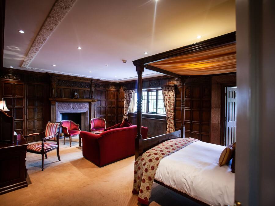 Quarto tradicional com cama de dossel, lareira e mobiliário de madeira clássico.