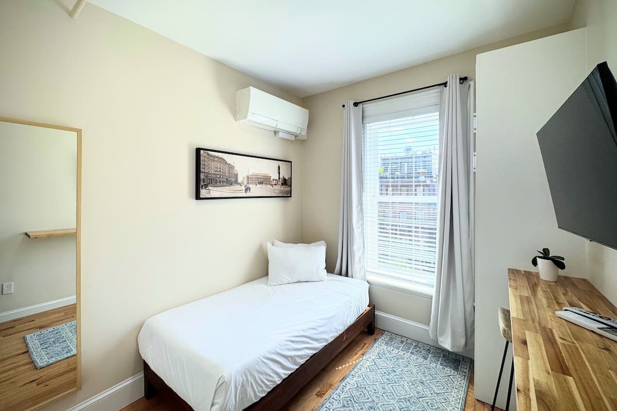 Quarto com cama, janela com cortinas, um quadro pendurado e uma televisão de tela plana.