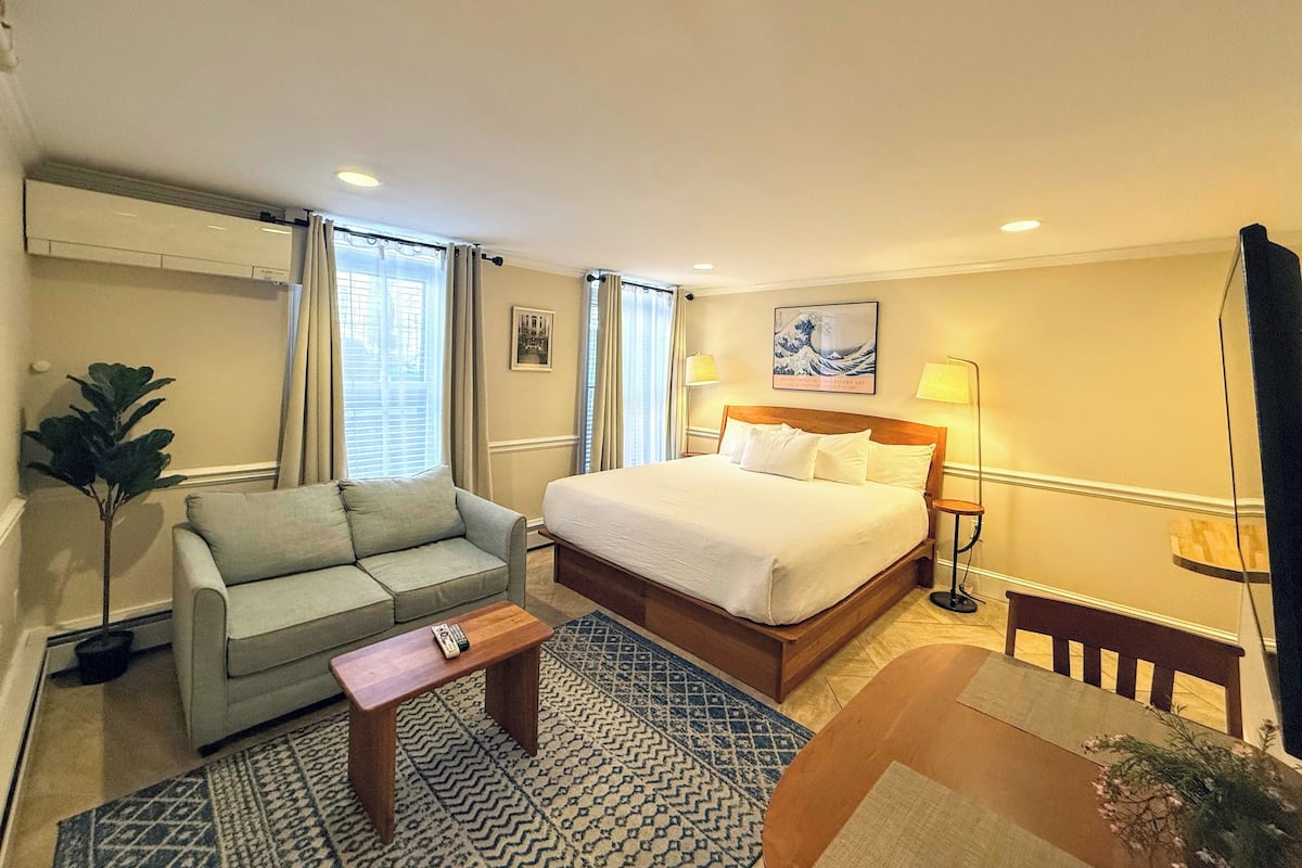 Quarto de hotel com cama, sofá, mesinha, luminária e planta.