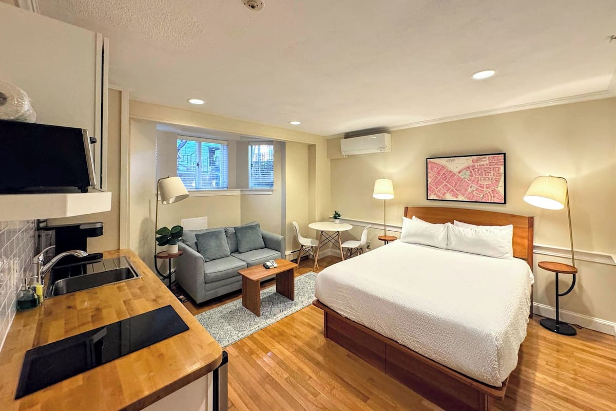 Quarto de hotel com cama, sofá, mesinha, televisão e janela.