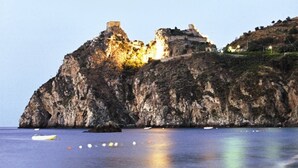 Um penhasco costeiro com ruínas históricas e um mar calmo.