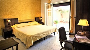 Quarto de hotel com cama, mesas de cabeceira, escrivaninha e cadeira, e vista para o exterior.