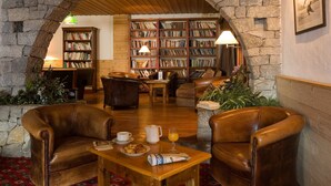 Uma biblioteca acolhedora com poltronas de couro, estantes e um arco de pedra.